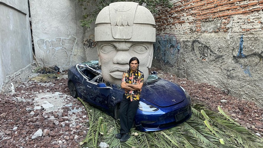 Artista esmaga carro Tesla com escultura colossal de cabeça olmeca