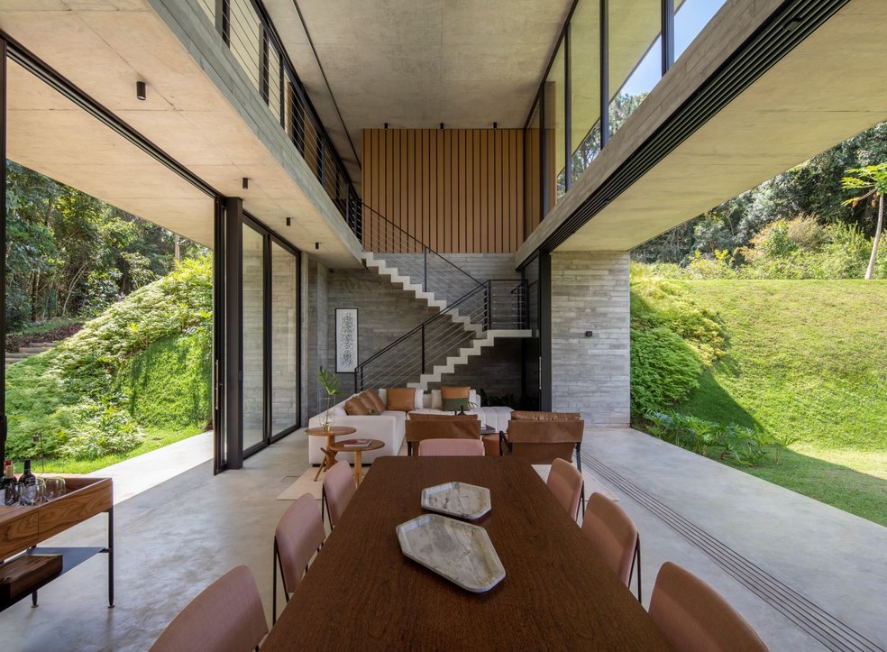 Casa em desnível na mata mistura vidro, concreto, madeira e caixilhos pretos